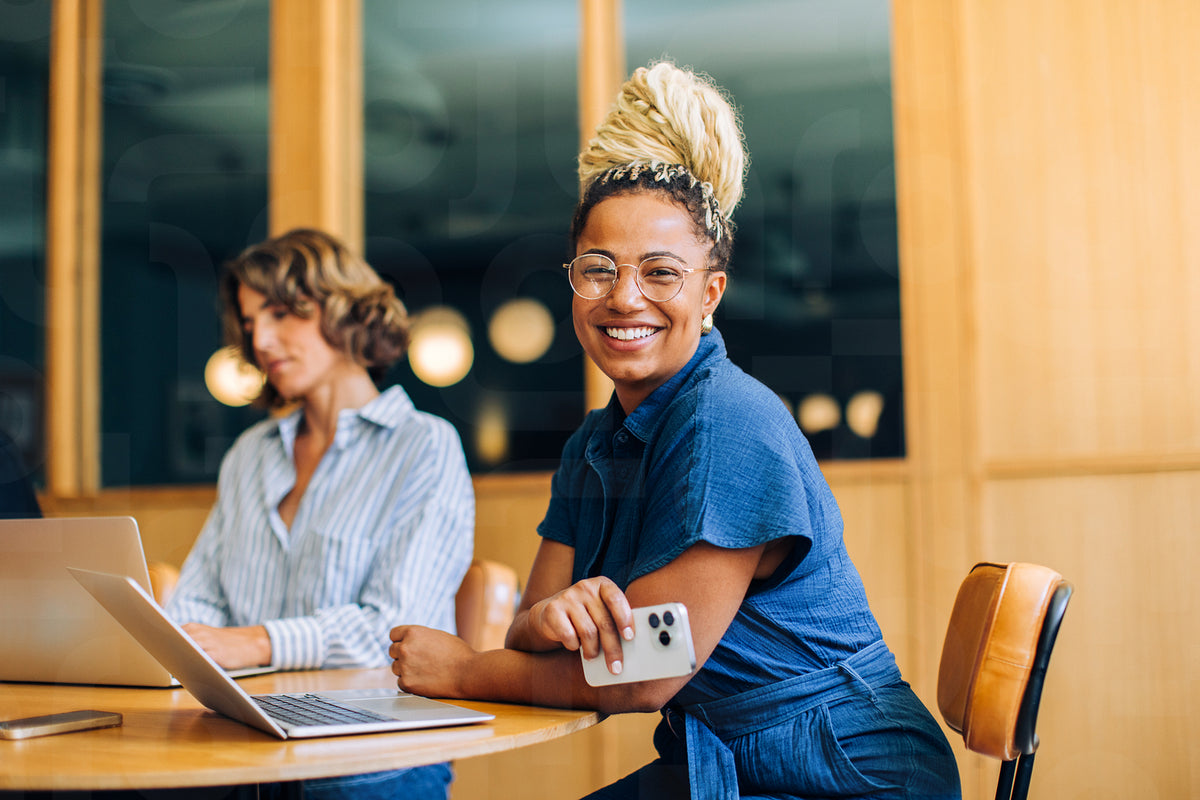 Two young women working and smiling in a bright, professional environm ...