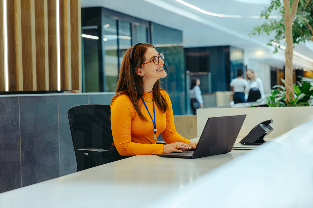 Smiling receptionist welcoming visitors at a modern company lobby ...