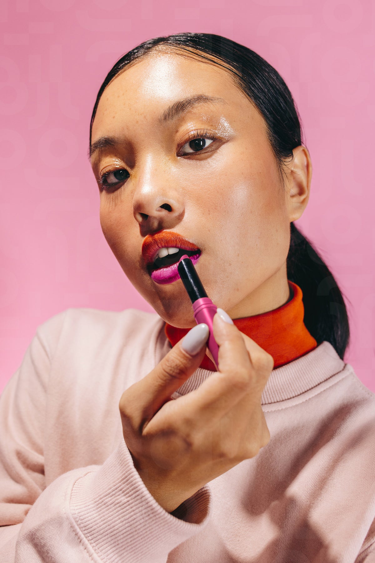 Going for a two-toned lip, young woman applies lipstick in a studio ...