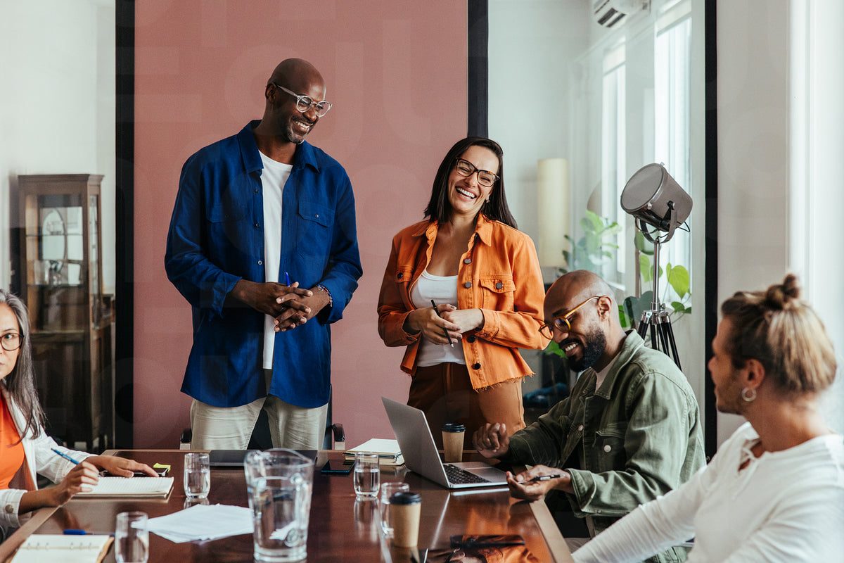 Creatives collaborating and laughing in a relaxed modern boardroom mee ...