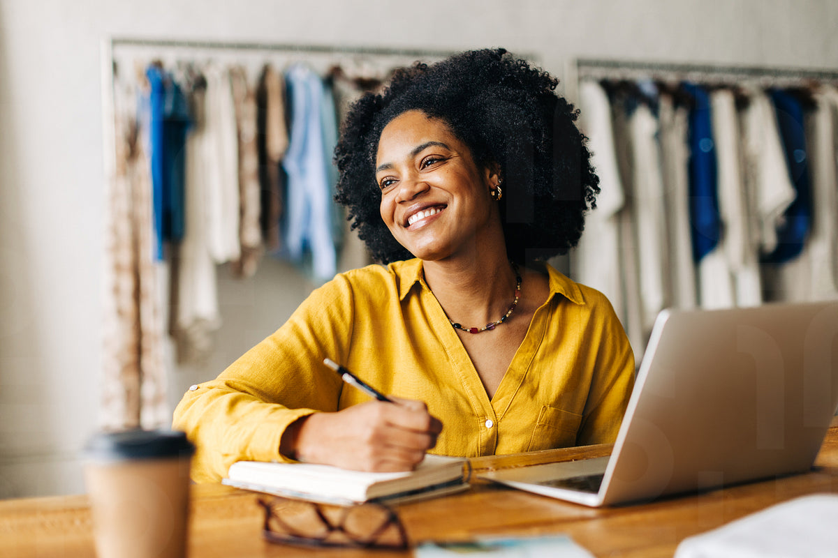 Happy fashion designer writing ideas for her small business in a note ...